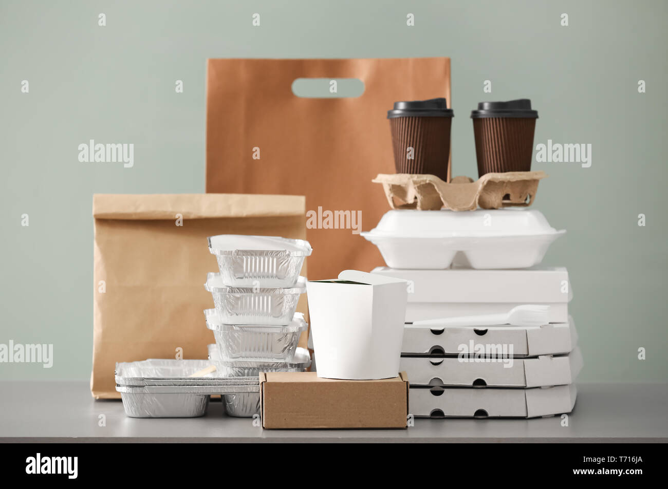 Different packages and carton cups on table against color background ...