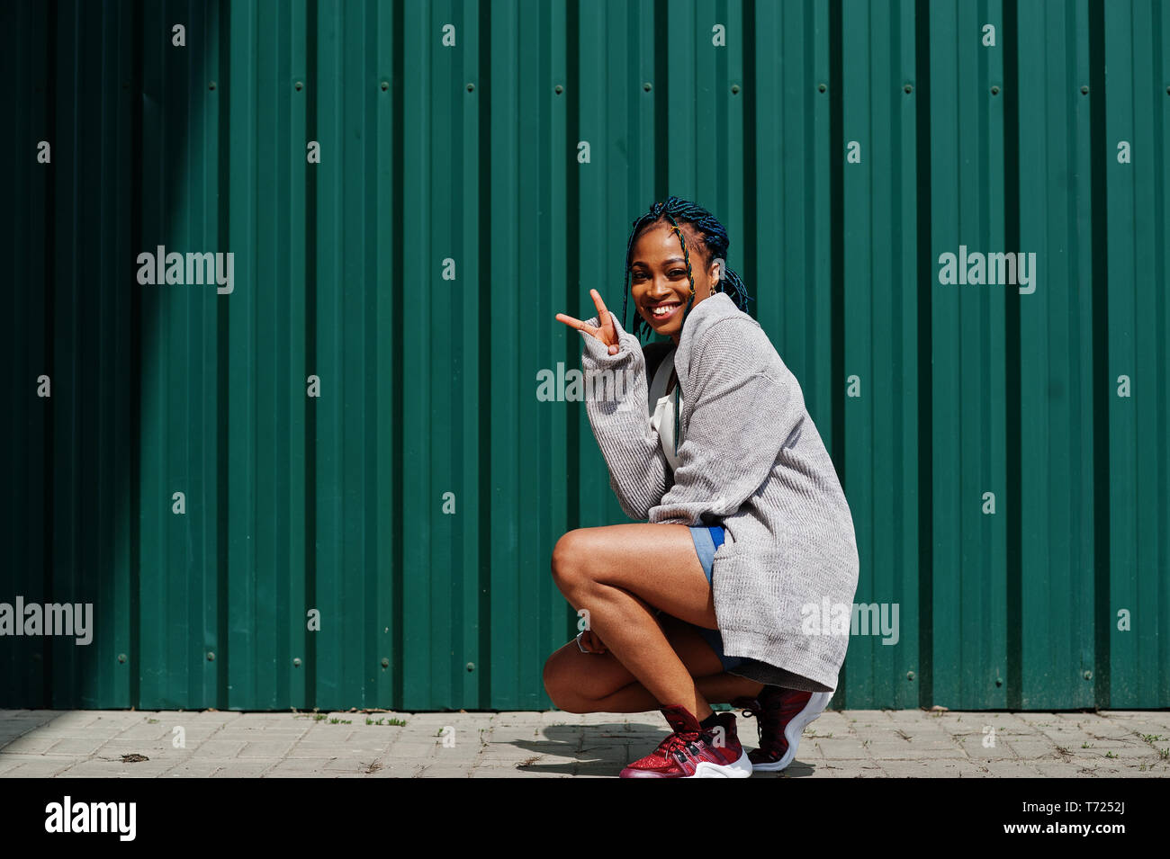 African woman with dreads hair, in jeans shorts crouching and show two ...