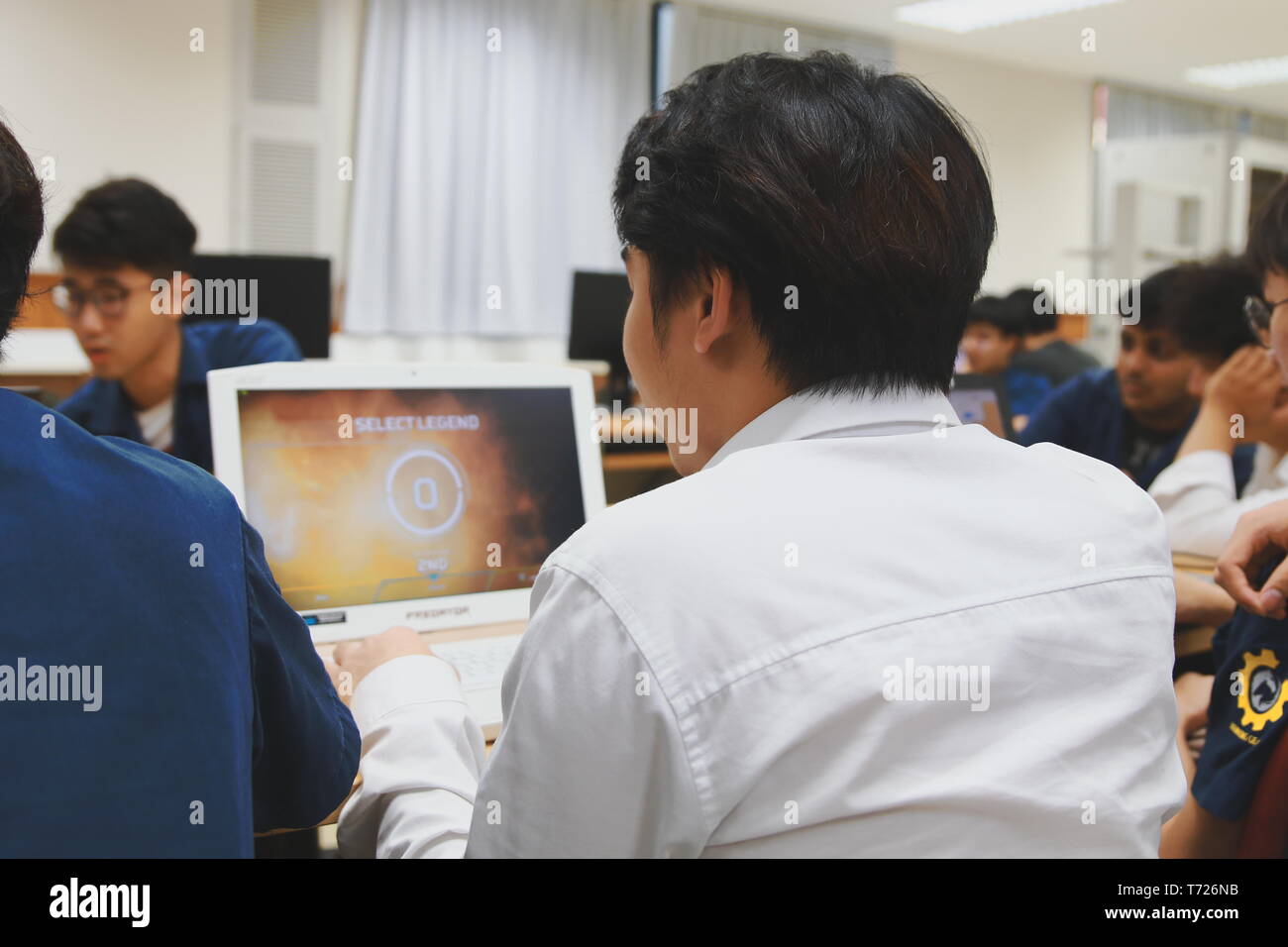 Asian university student playing game on his laptop in the classroom ...