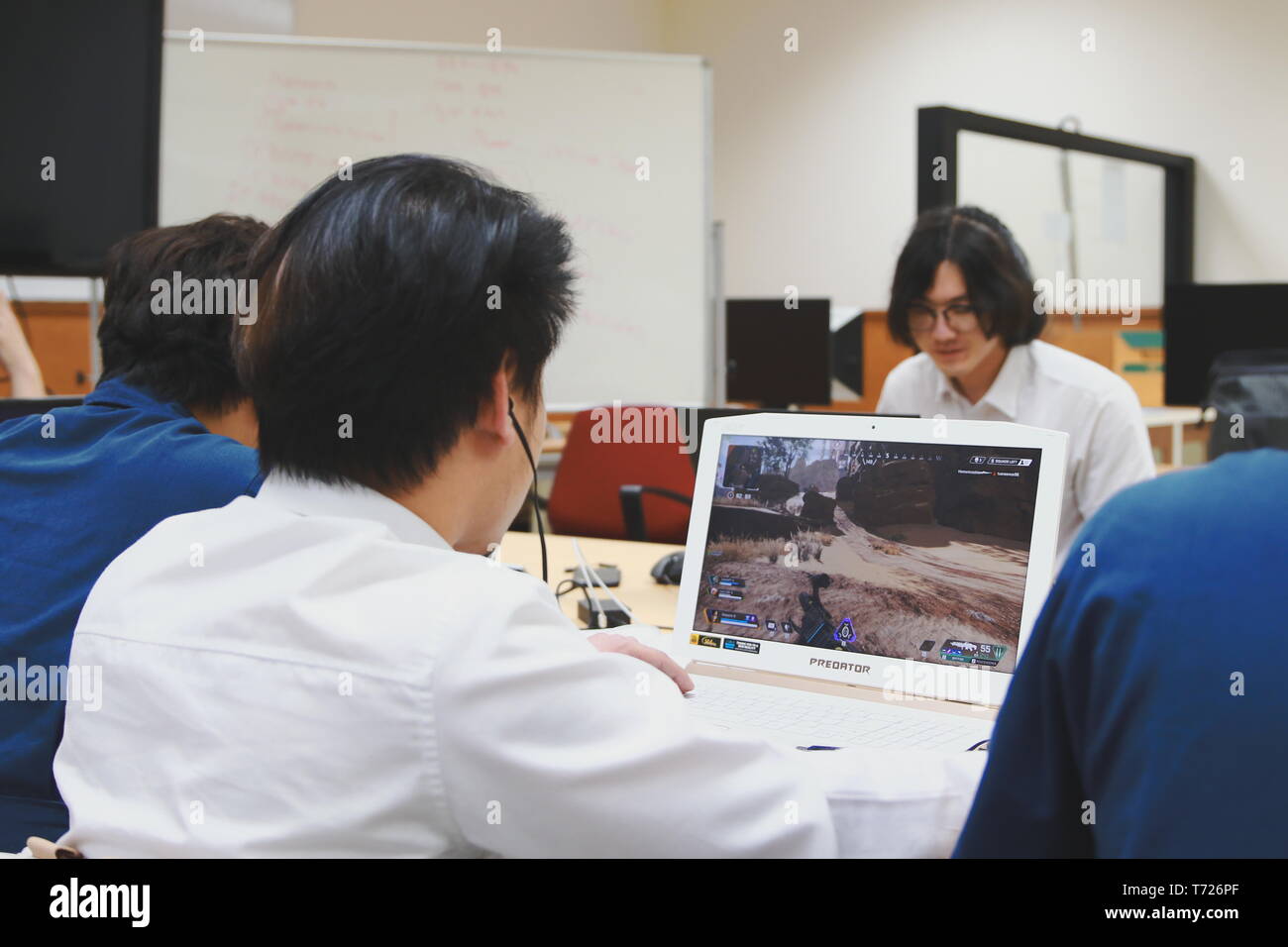 Asian university student playing game on his laptop in the classroom ...