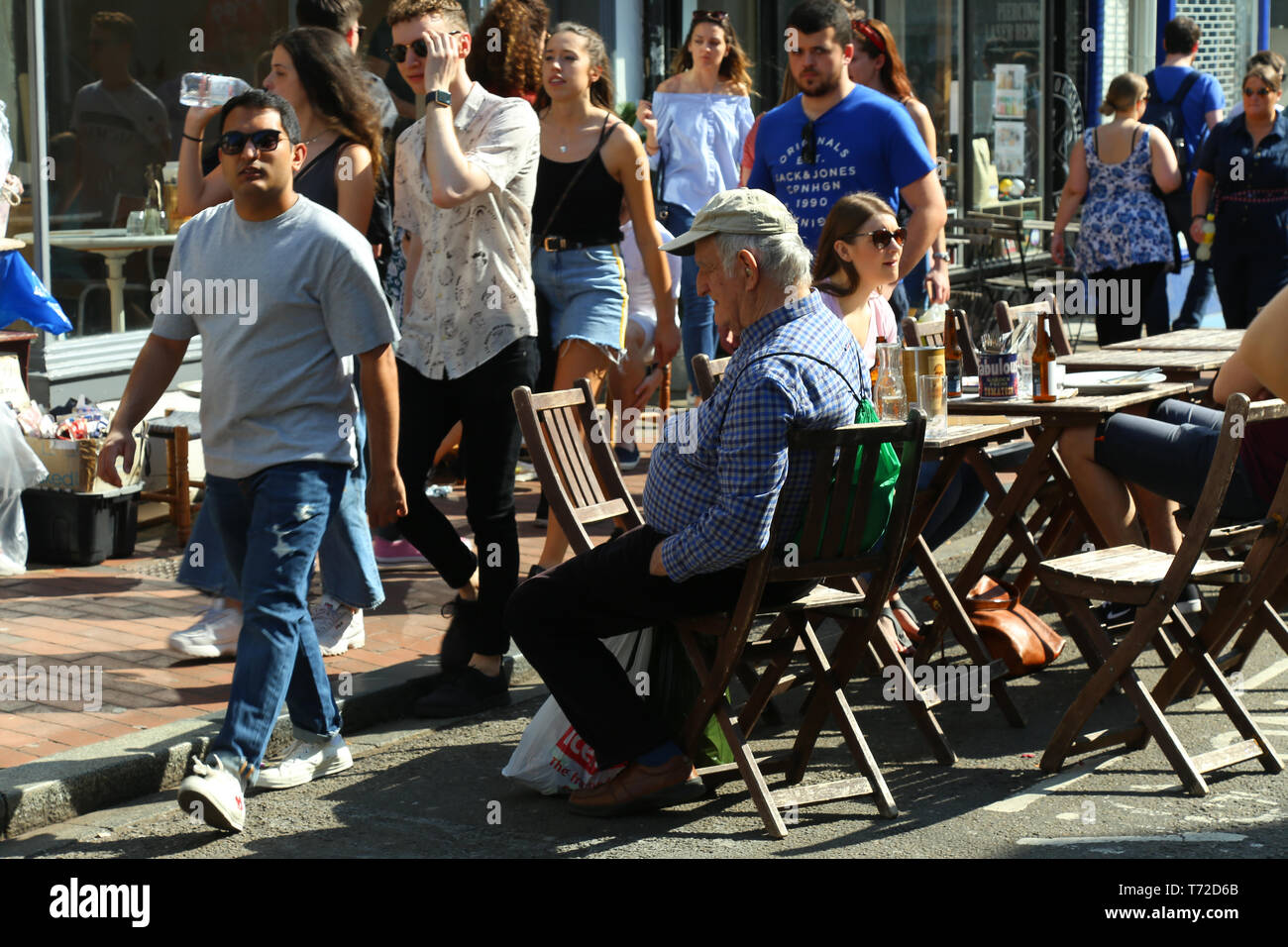 People walking in from an old man seated on the chair on the street ...