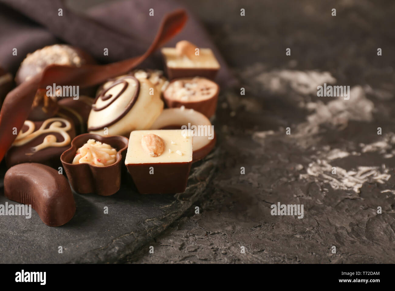 Slate plate with different tasty chocolate candies on textured table ...