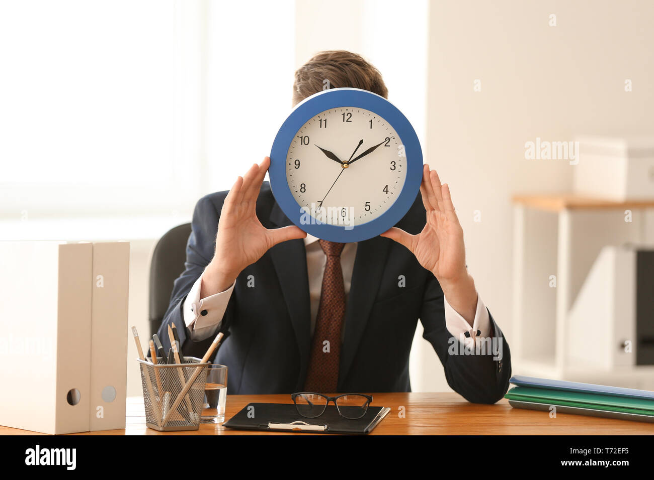 Man hiding face behind clock at table in office. Time management ...