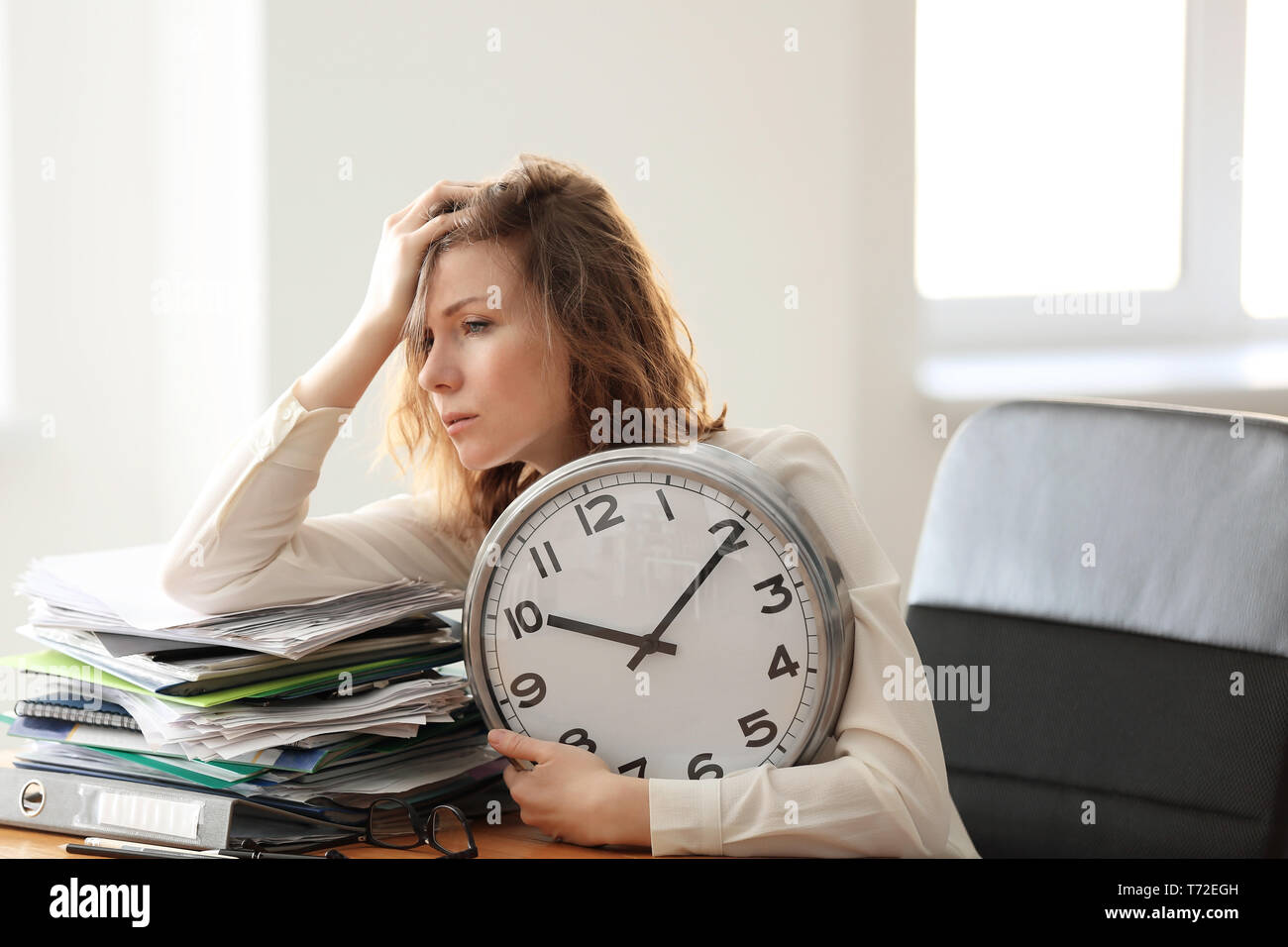 Mature tired woman with clock at table in office. Time management ...