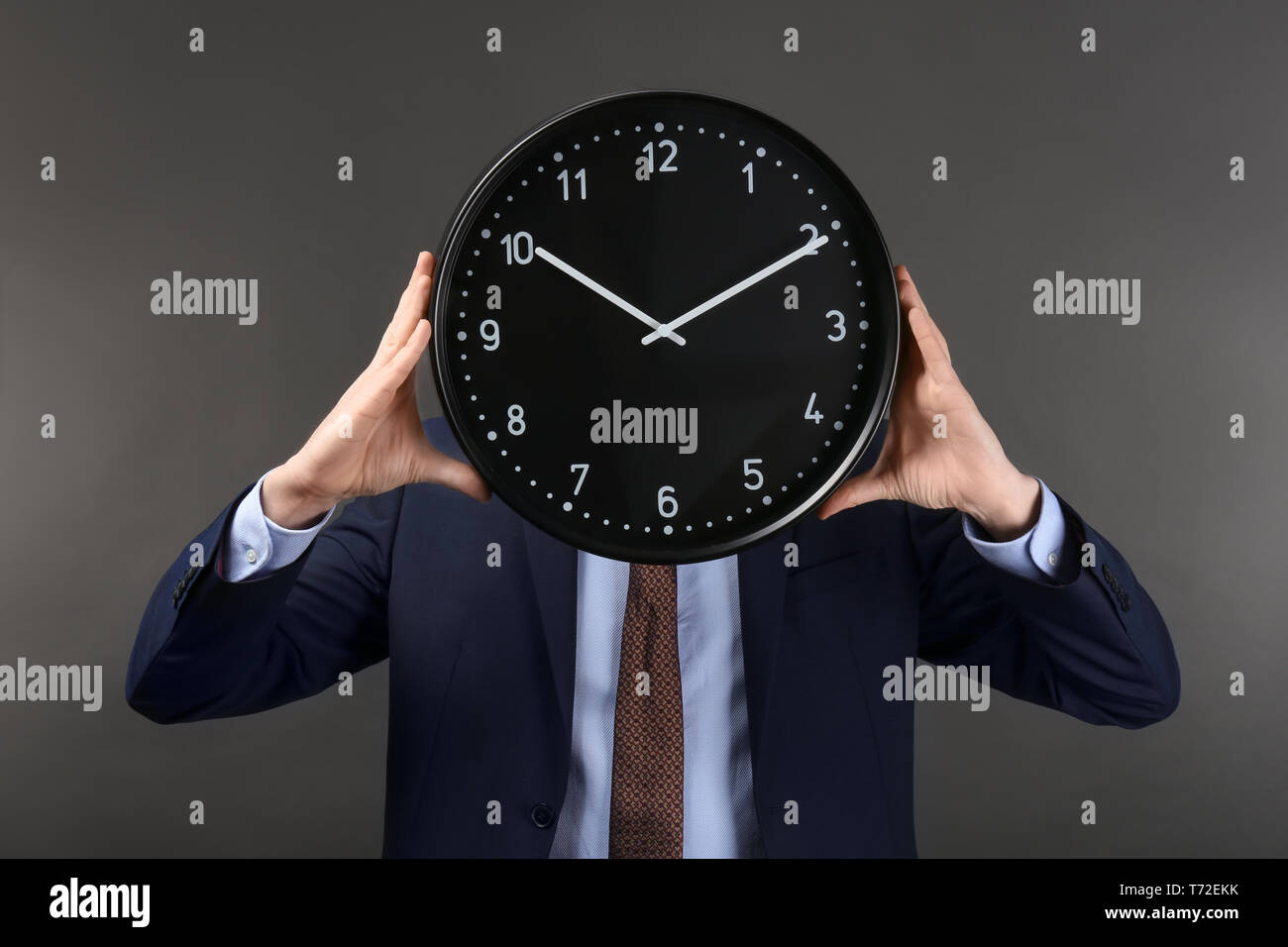 Man hiding face behind clock on dark background. Time management ...