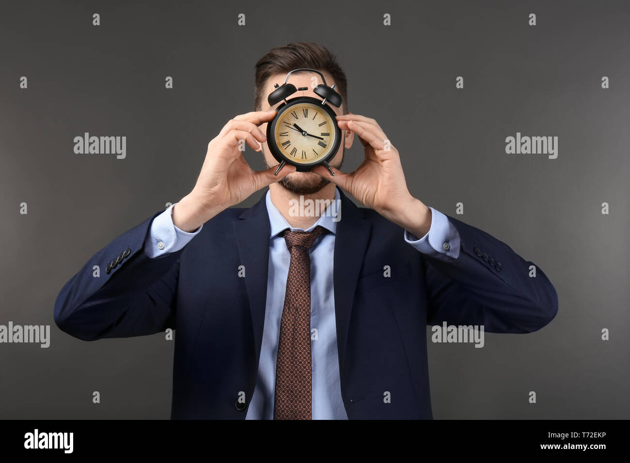 Man hiding face behind alarm clock on dark background. Time management ...