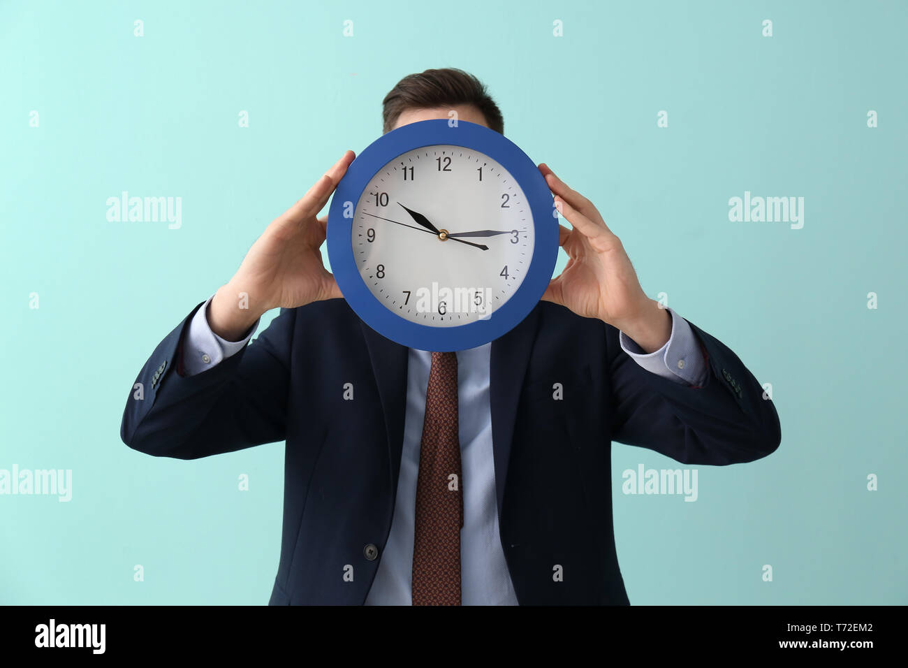 Man hiding face behind clock on color background. Time management ...