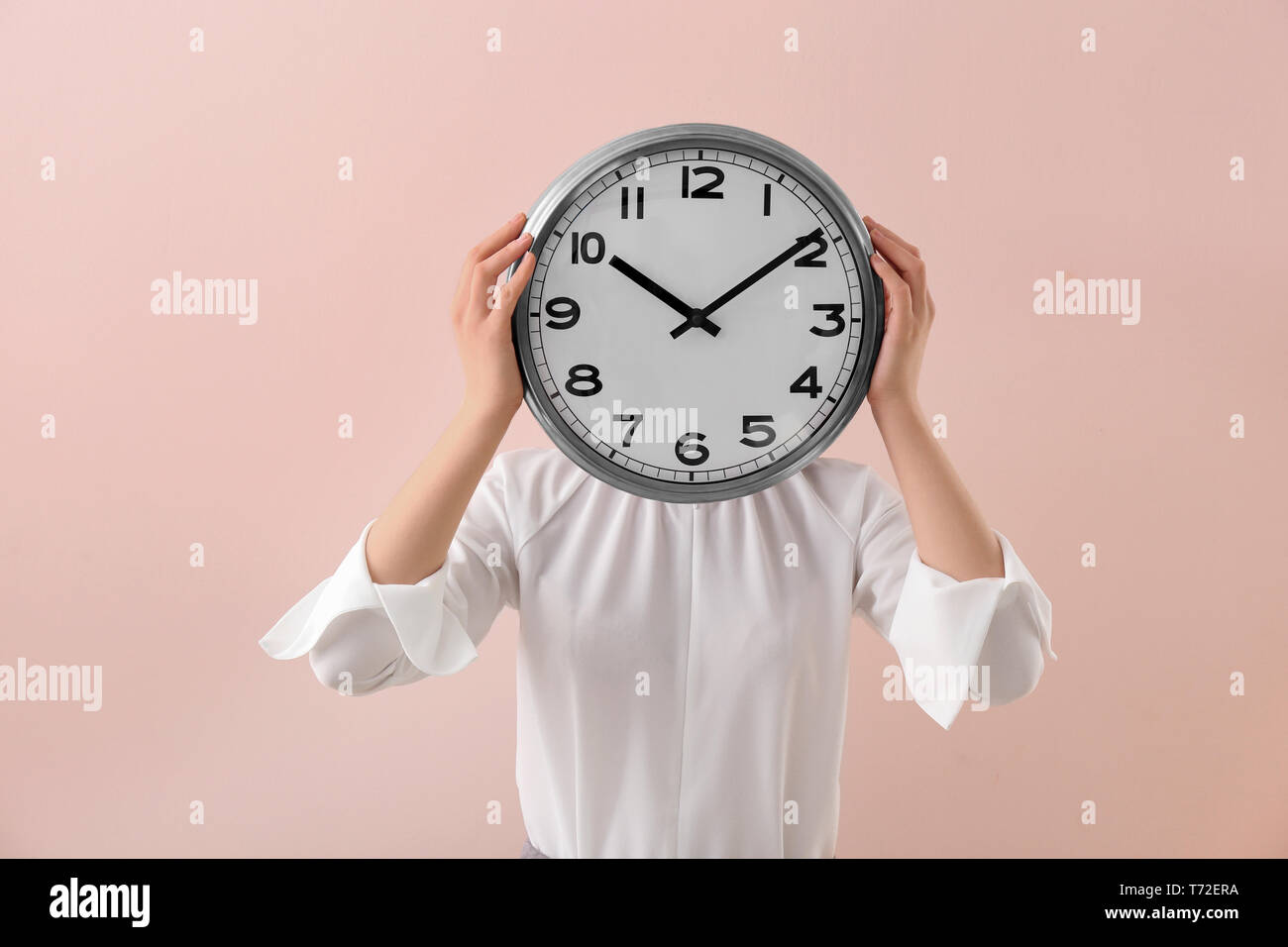 Woman hiding face behind clock on color background. Time management ...