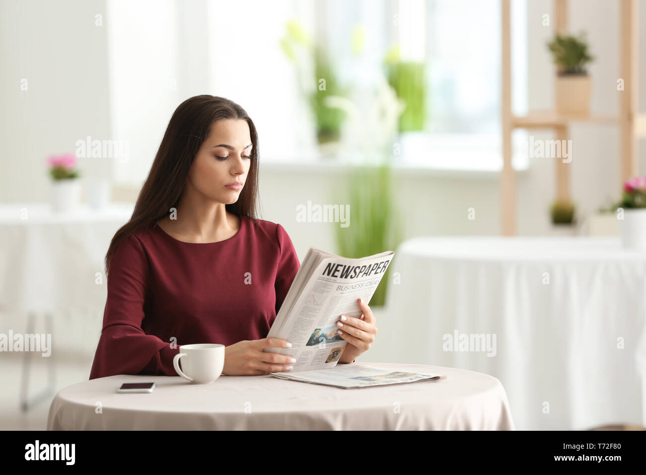 Young woman reading newspaper in cafe Stock Photo - Alamy