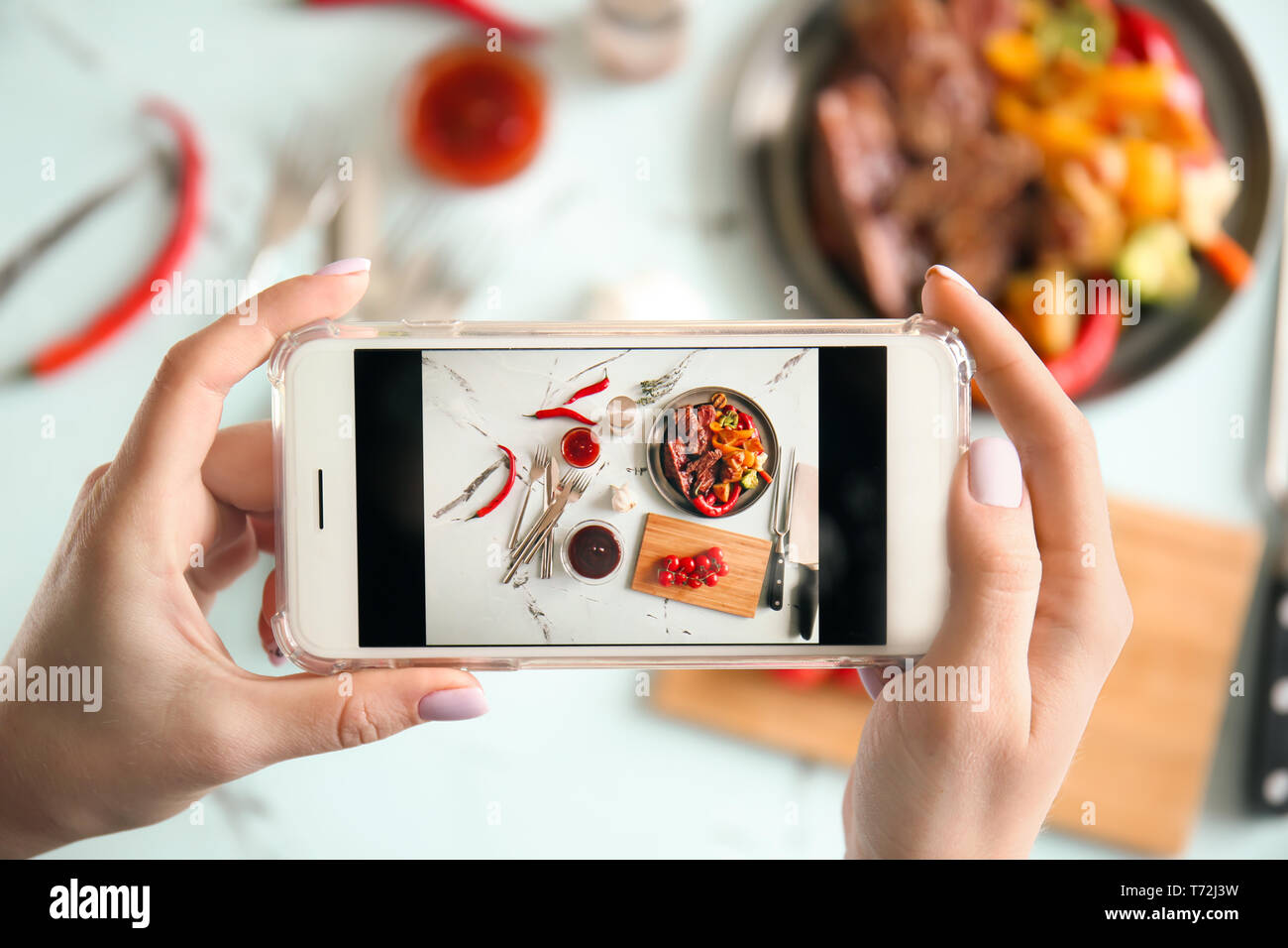Woman taking photo of barbecue sauce and grilled meat with mobile phone ...