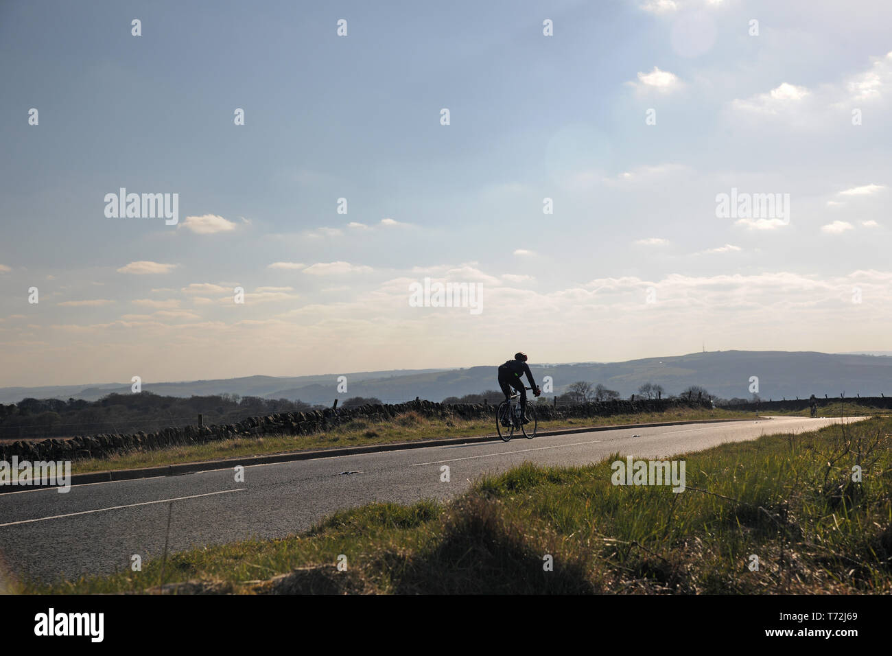 Cyclist riding along a country road in the Peak District, with hills in ...