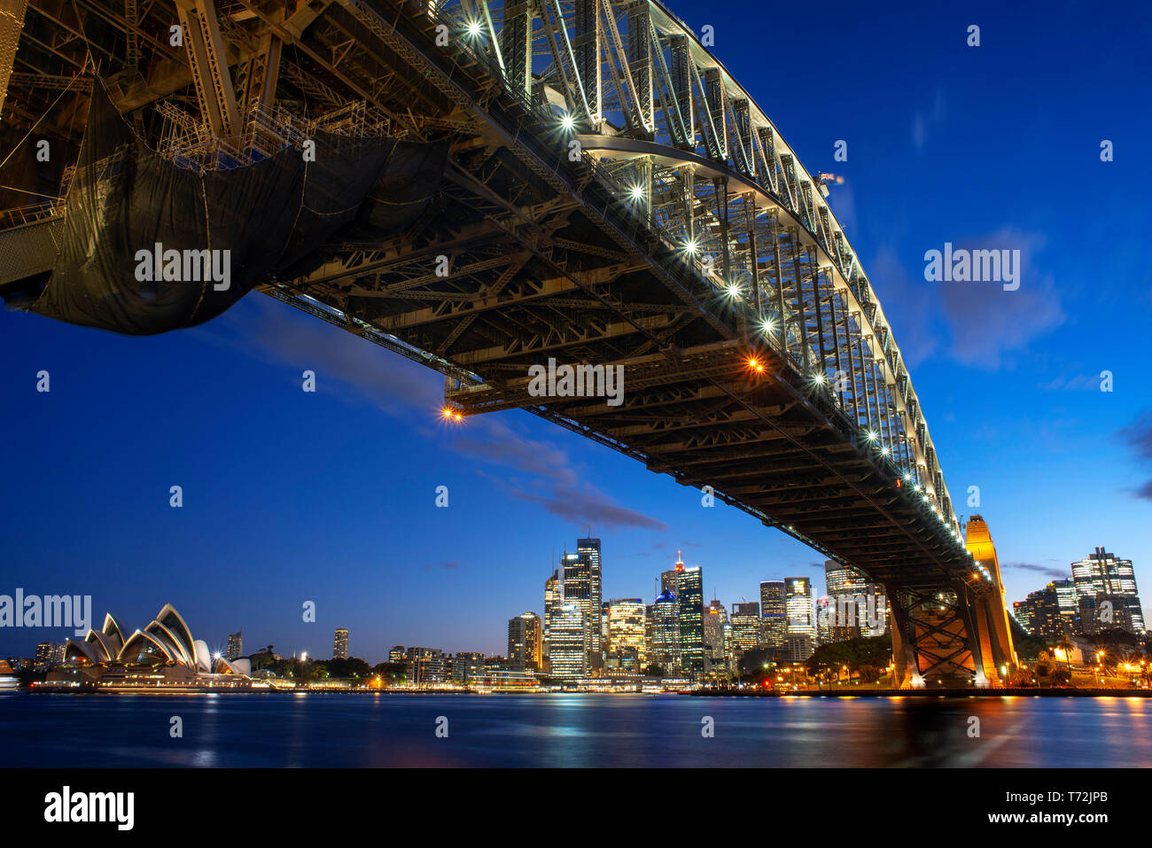 Side view of Sydney Harbour bridge Opera House and city CBD at sunset. Illuminated arch of the ...