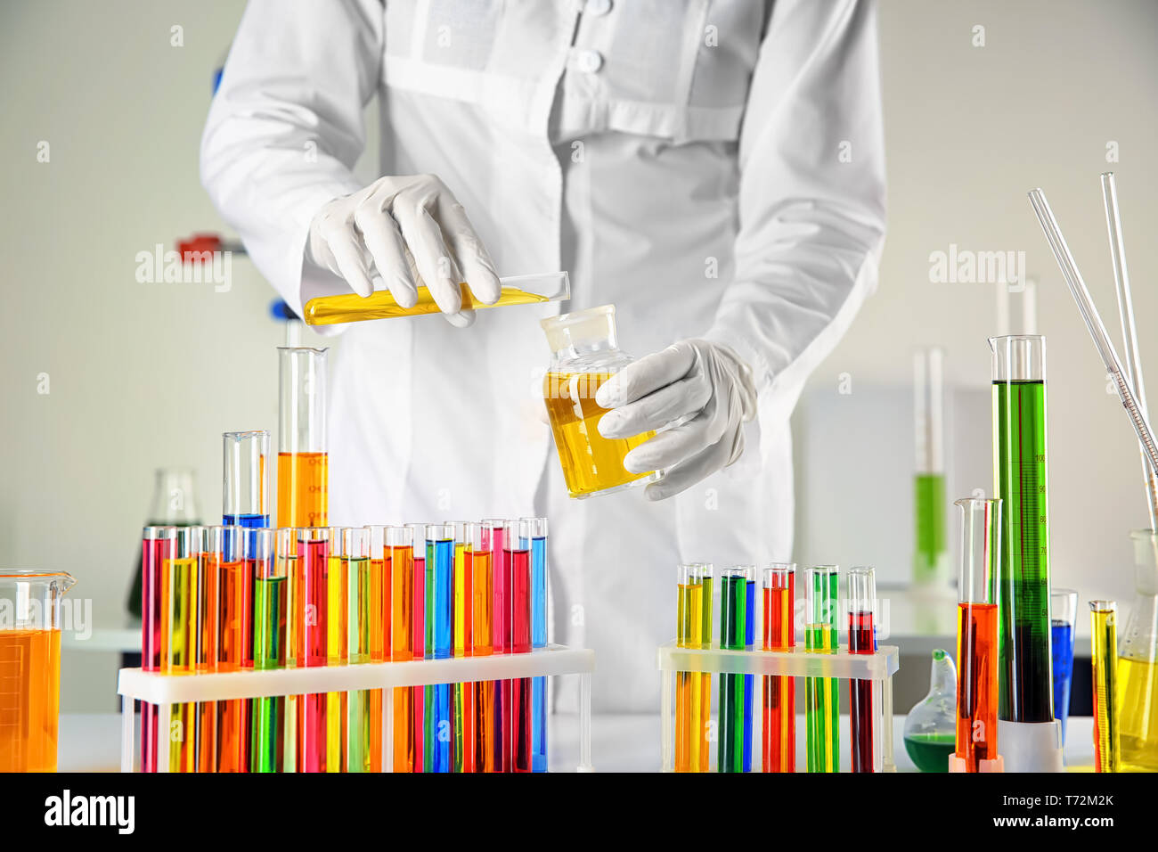 Laboratory assistant pouring liquid from test tube into flask over ...