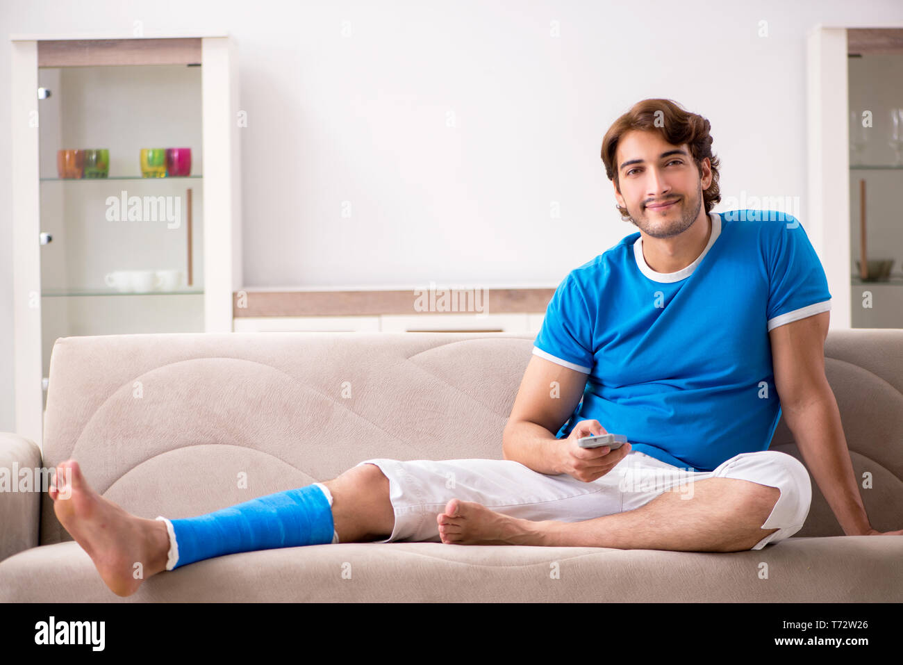 Leg injured young man on the sofa Stock Photo - Alamy
