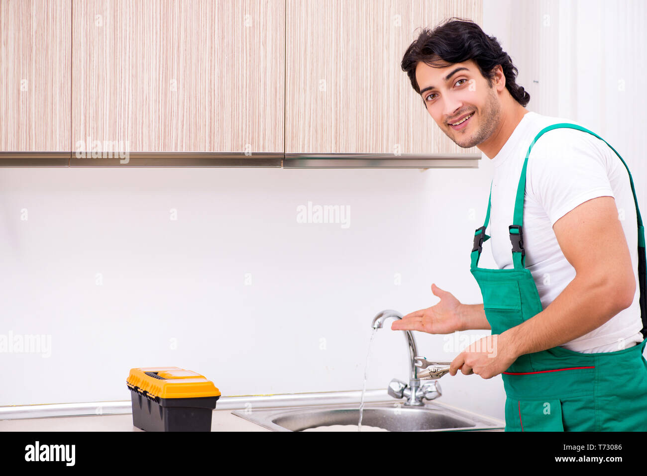 Young plumber repairing tap at kitchen Stock Photo - Alamy