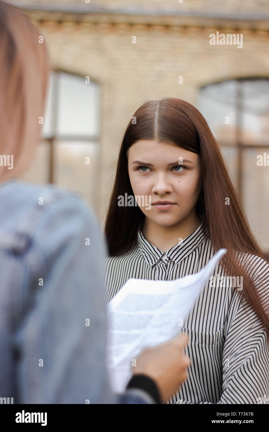 Girl is standing near the university and look at the adult with paper ...
