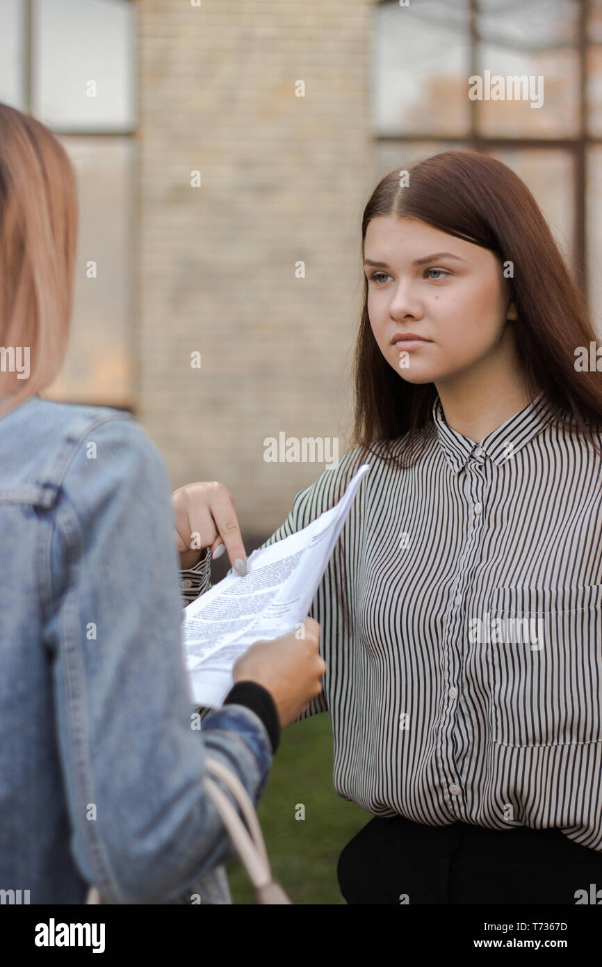 Unhappy girl is standing near the university and points to paper ...