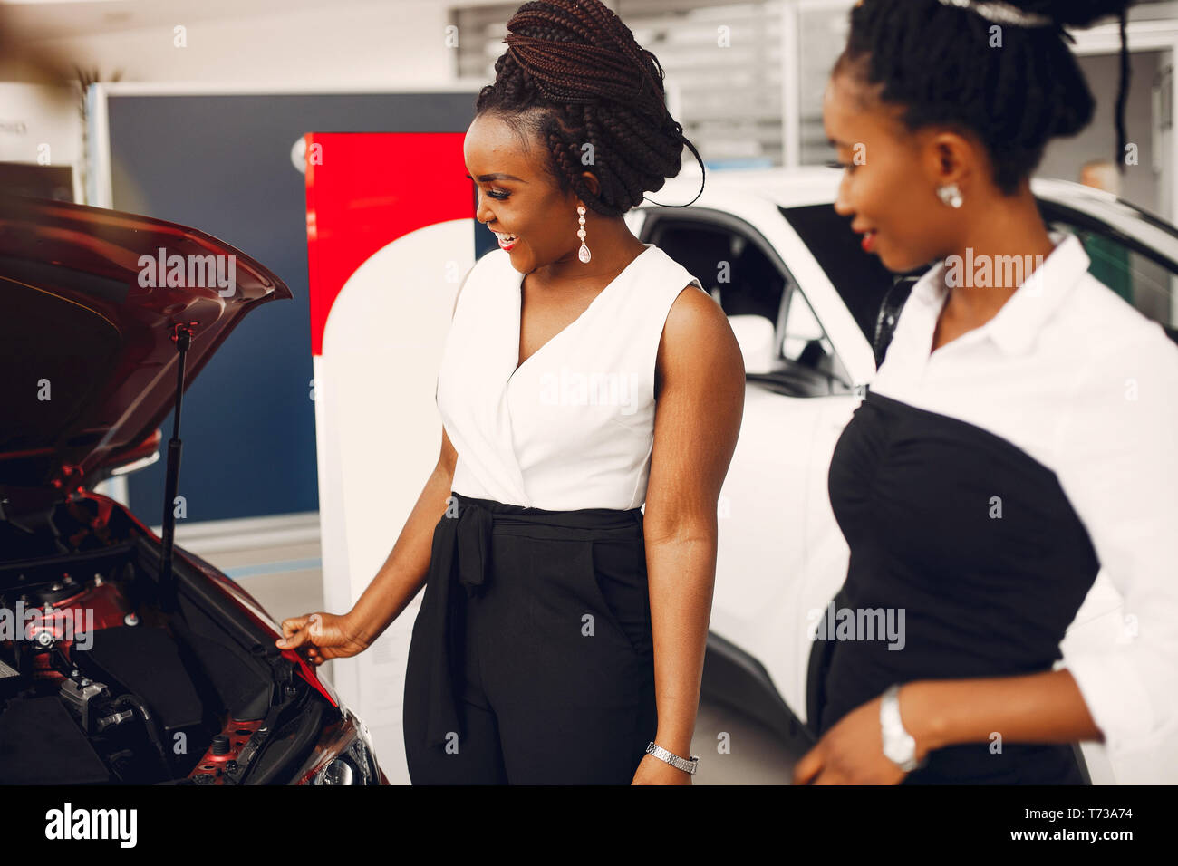 Women buying the car. Ladies in a car salon. Black girls near red car ...