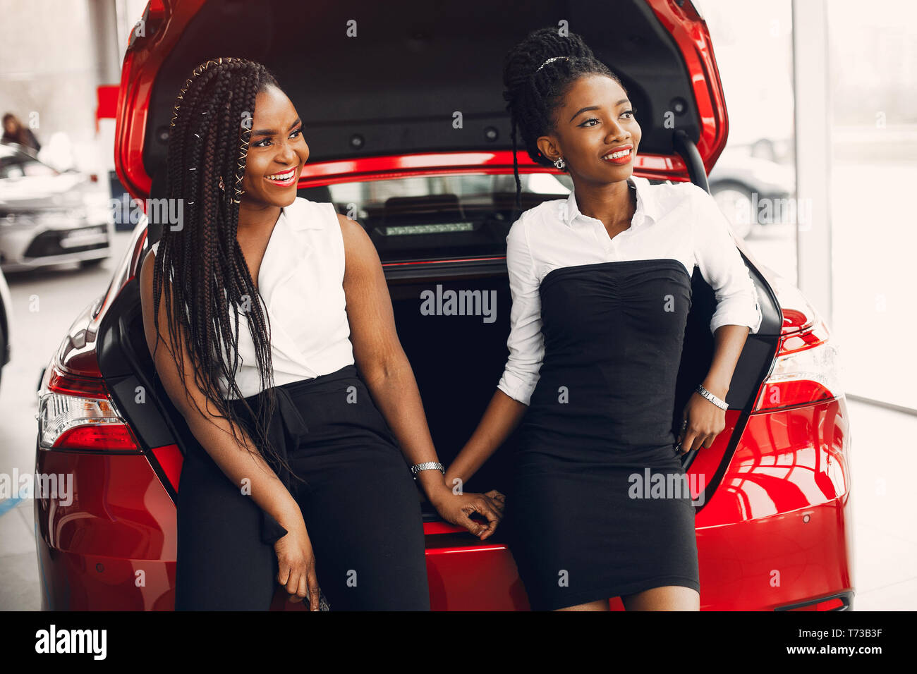 Women buying the car. Ladies in a car salon. Black girls near red car ...