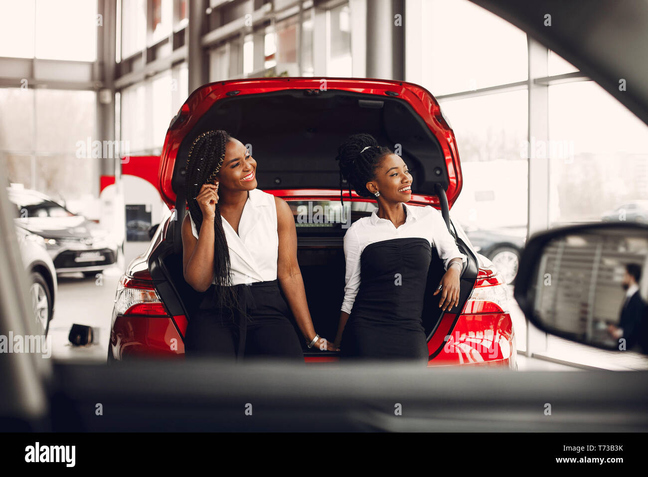 Women buying the car. Ladies in a car salon. Black girls near red car ...