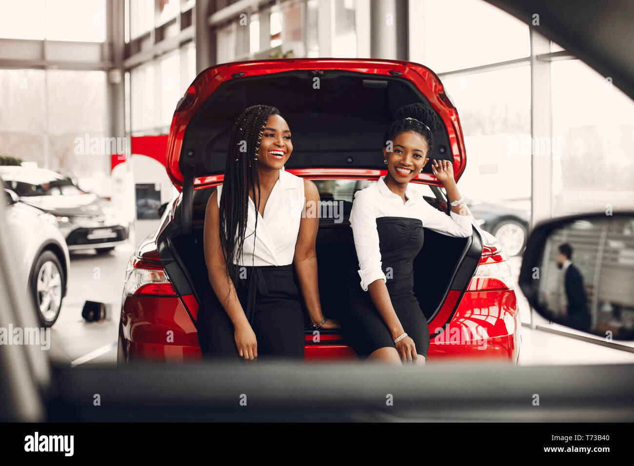 Women buying the car. Ladies in a car salon. Black girls near red car ...