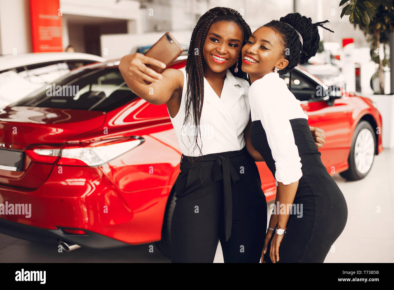 Women buying the car. Ladies in a car salon. Black girls near red car ...