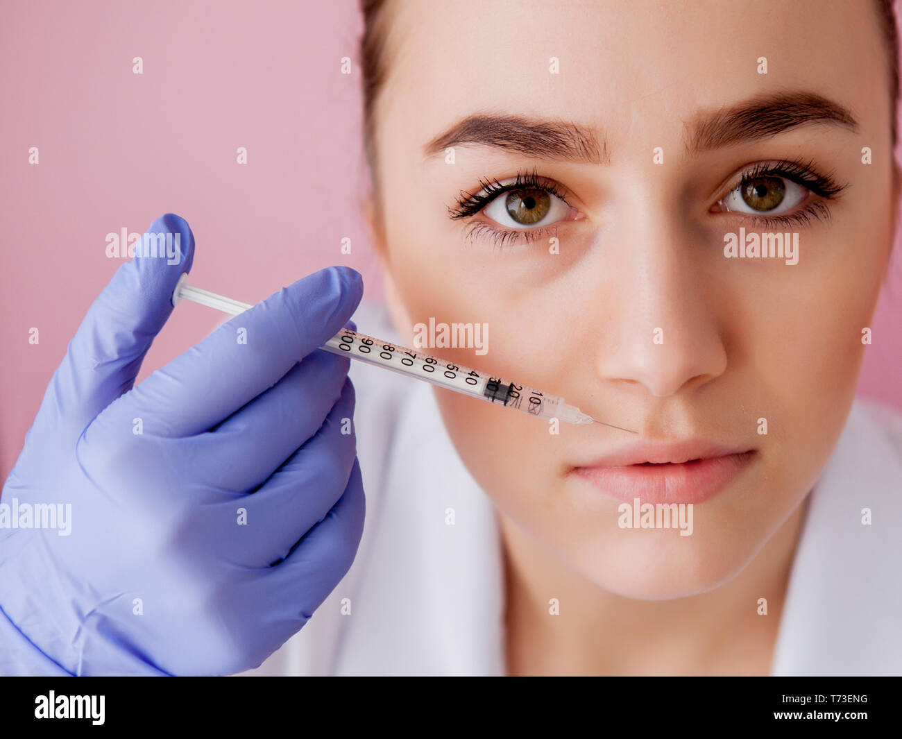 Doctor in gloves giving woman botox injections in lips, on pink ...
