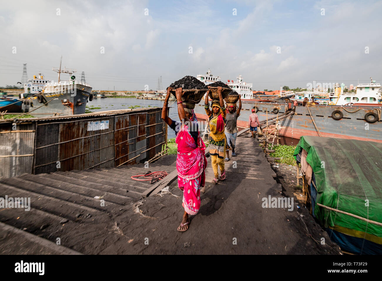 Male & Female dock workers are seen as they unload coal with bamboo ...