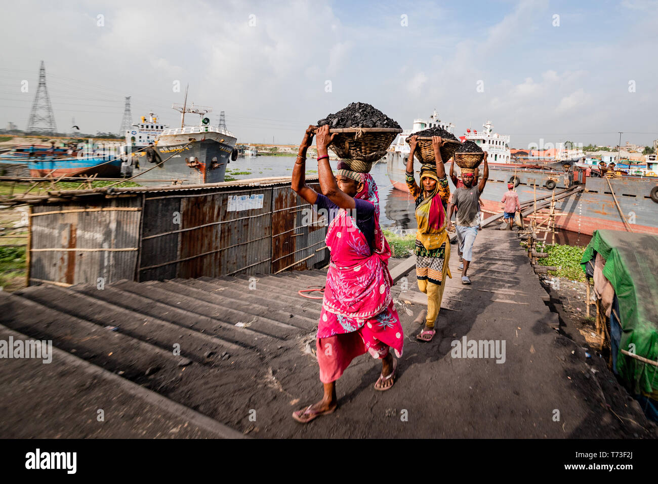Male & Female dock workers are seen as they unload coal with bamboo ...