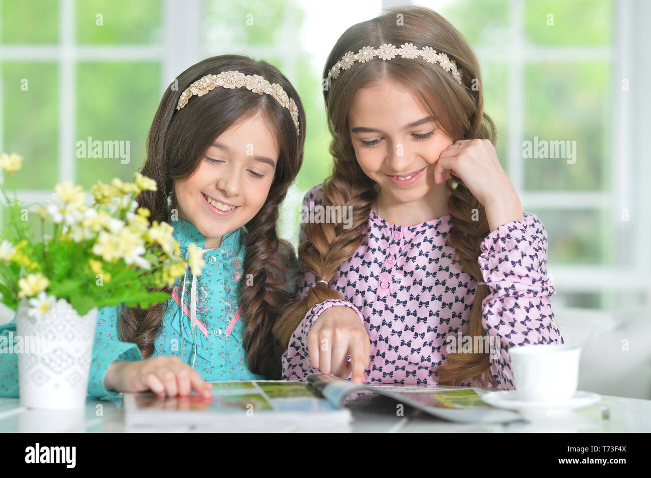 Portrait of two cute girls reading magazine Stock Photo - Alamy
