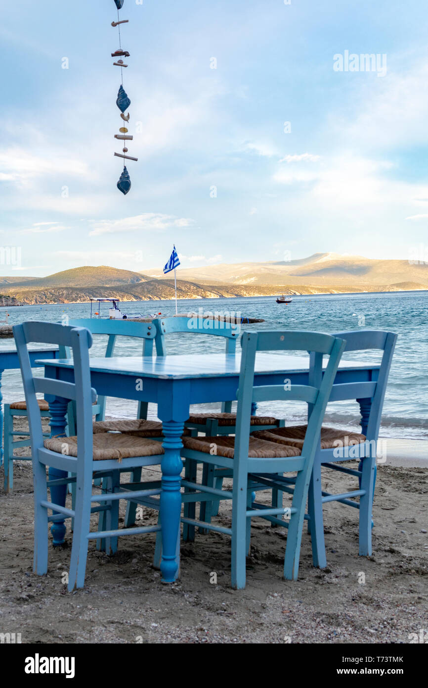 Traditional greek tavern with wooden tables on sandy beach near water ...