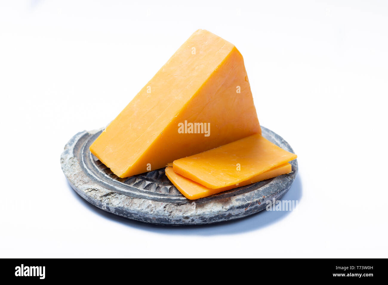Piece of hard orange Cheddar cheese on grey stone plate isolated, close ...