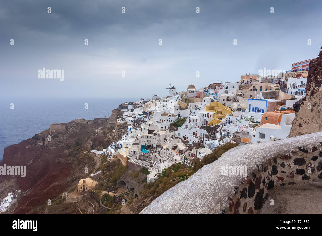 View of colorful houses of Oia and red cliffs on a rare rainy day ...
