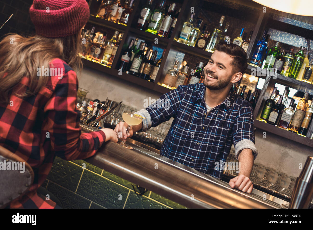 Young barman standing at bar counter serving woman with cocktail ...