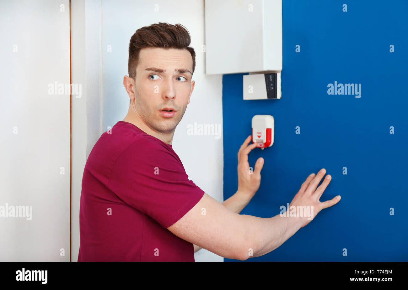 Frightened man using fire alarm system indoors Stock Photo - Alamy