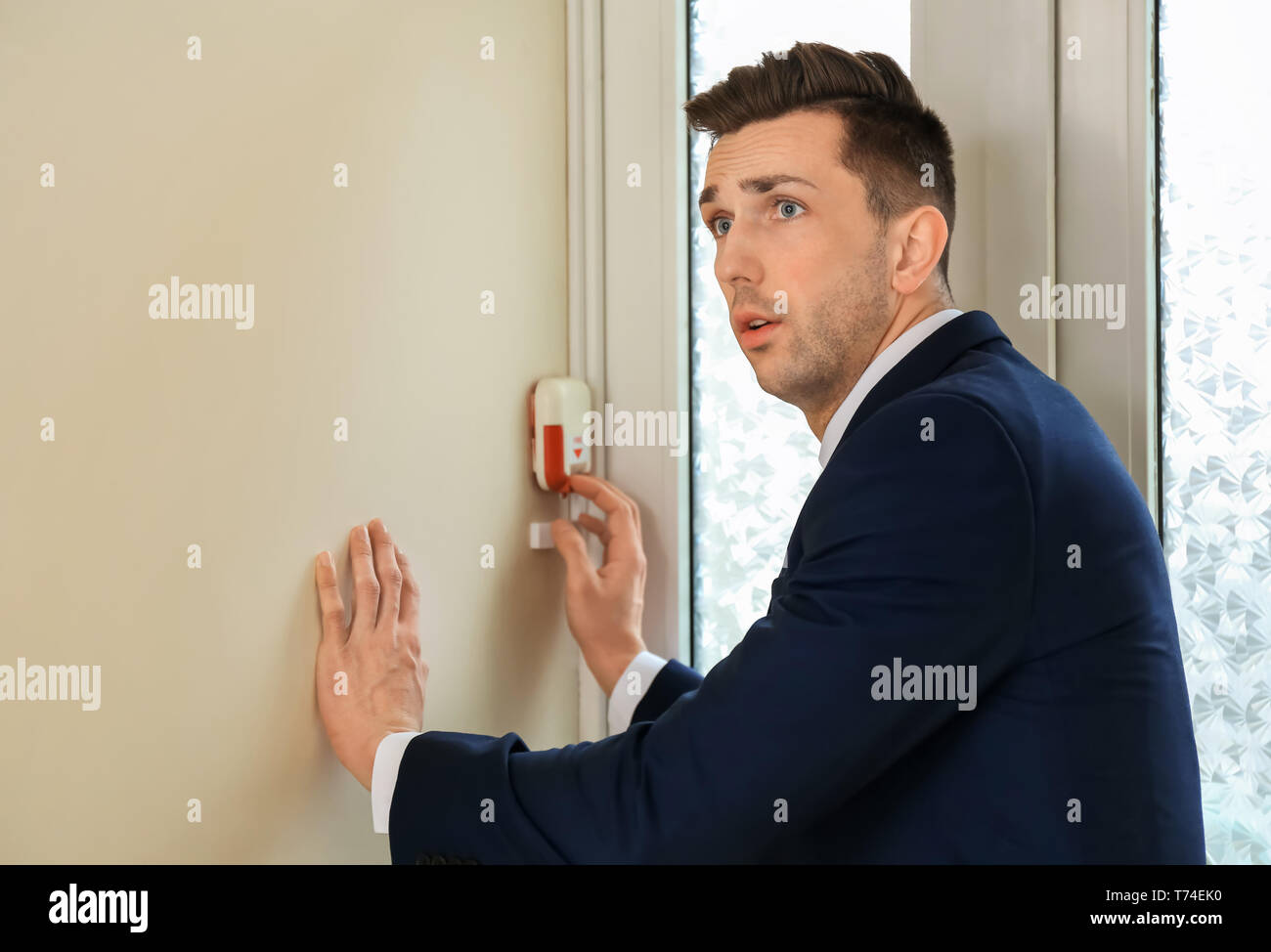 Frightened man using fire alarm system indoors Stock Photo - Alamy