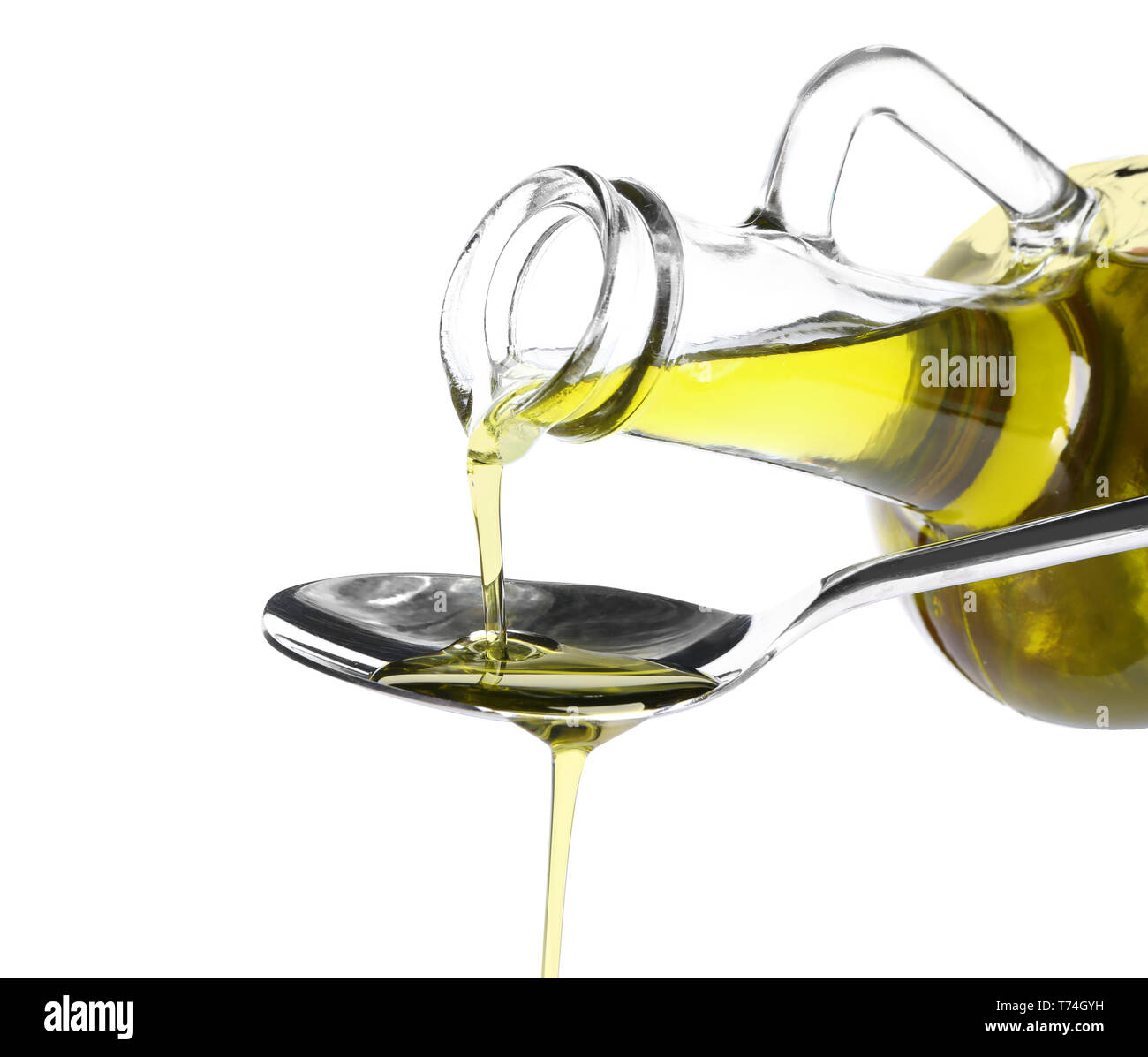 Pouring of olive oil from glass jug into spoon on white background ...