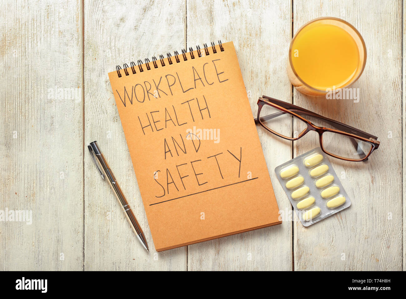 Words "Workplace, health and safety" written in notebook, glass of ...