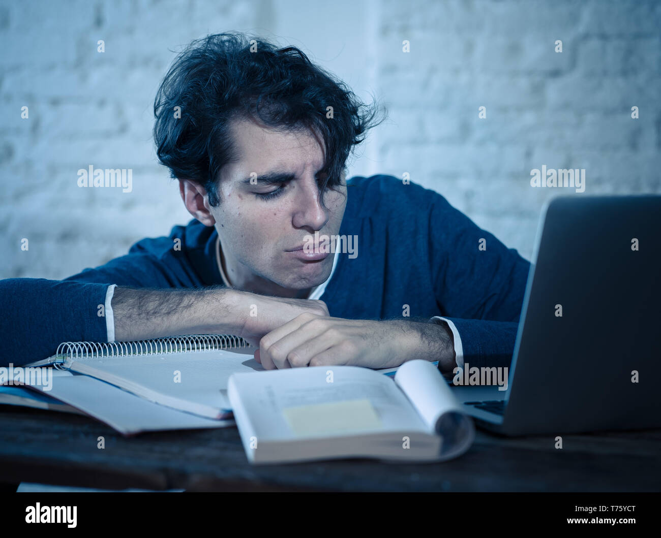Overworked and tired male student working late at night on laptop ...