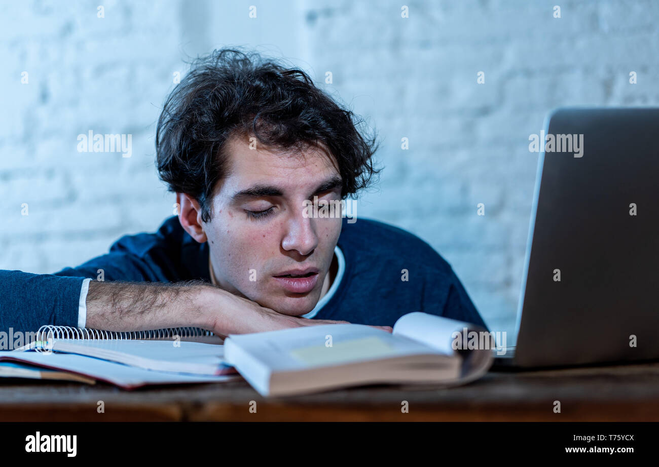 Overworked and tired male student working late at night on laptop ...