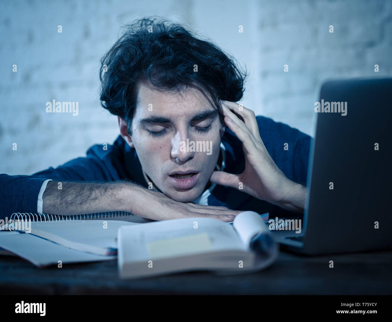 Overworked and tired male student working late at night on laptop ...