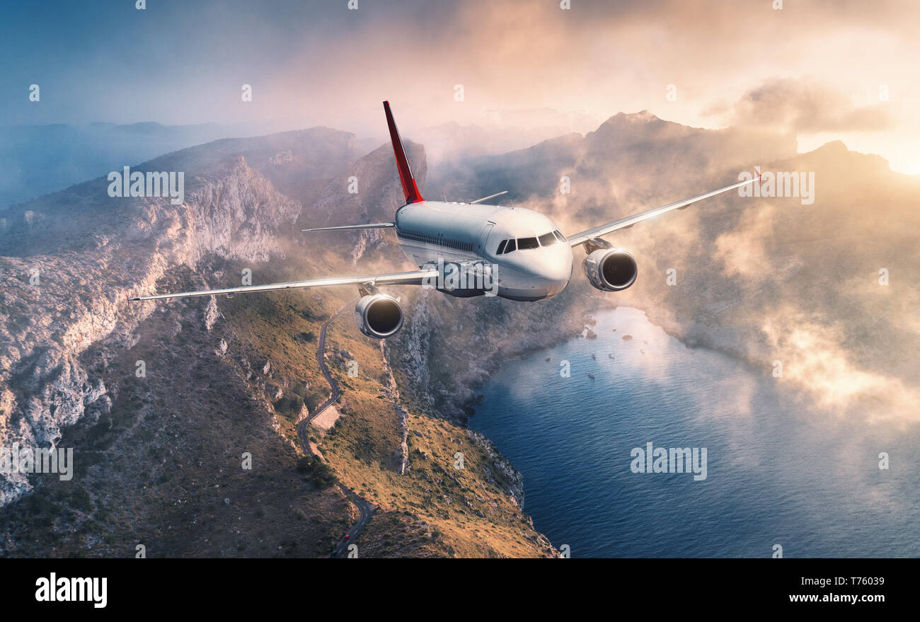 Airplane is flying over mountains and low clouds at sunset in summer ...