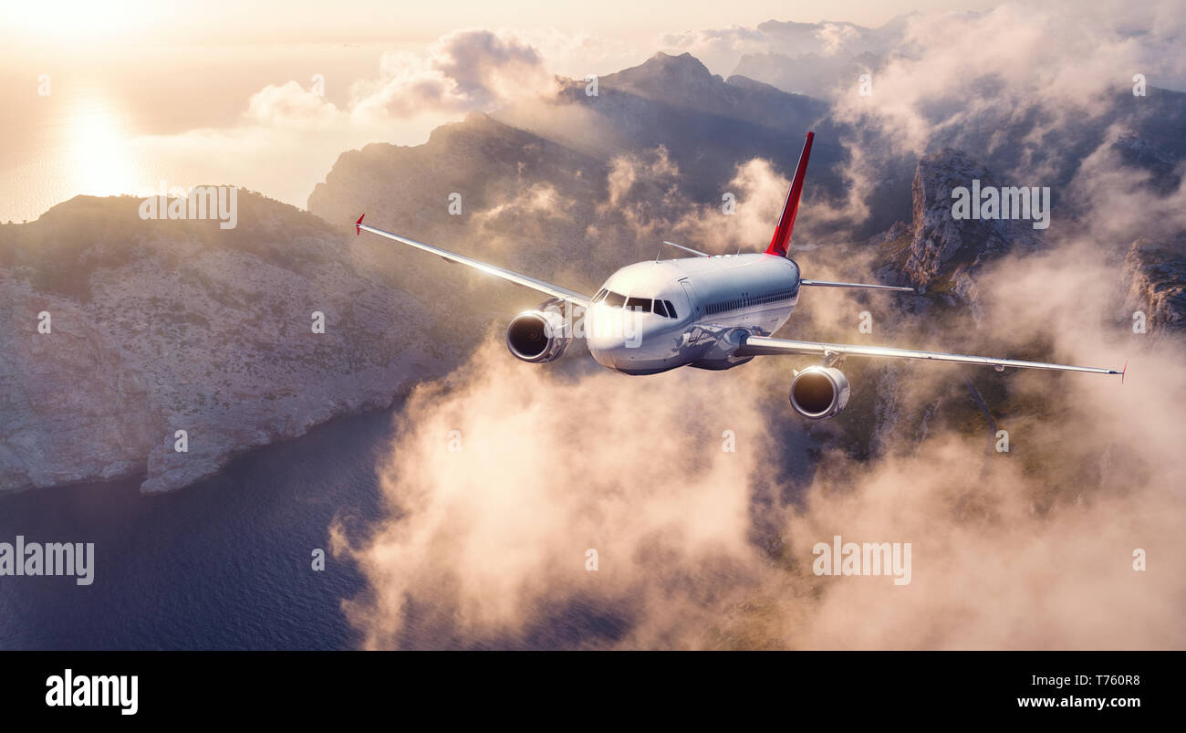 Airplane is flying over mountains and low clouds at sunset in summer ...