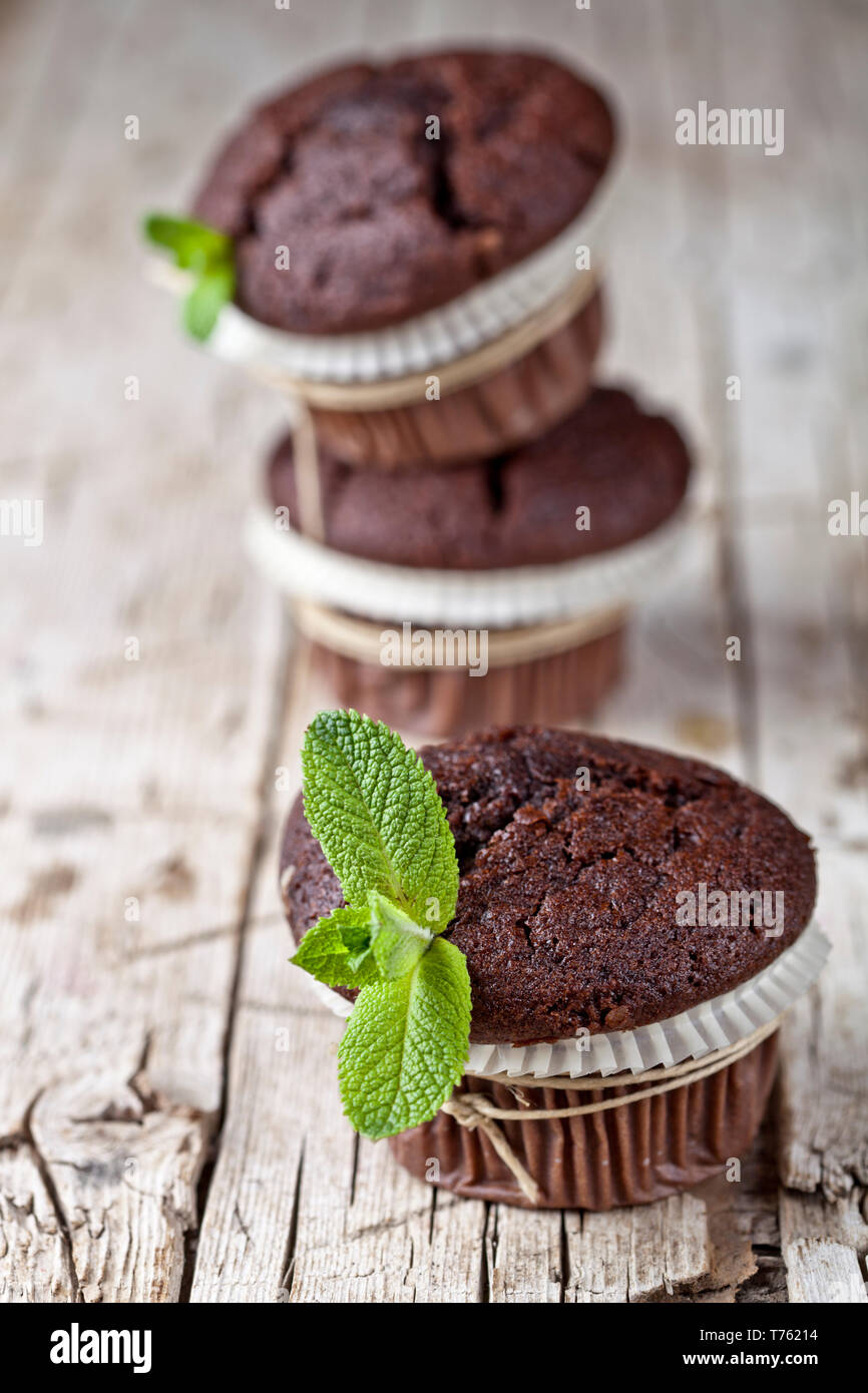 Three fresh dark chocolate muffins with mint leaves on rustic wooden ...