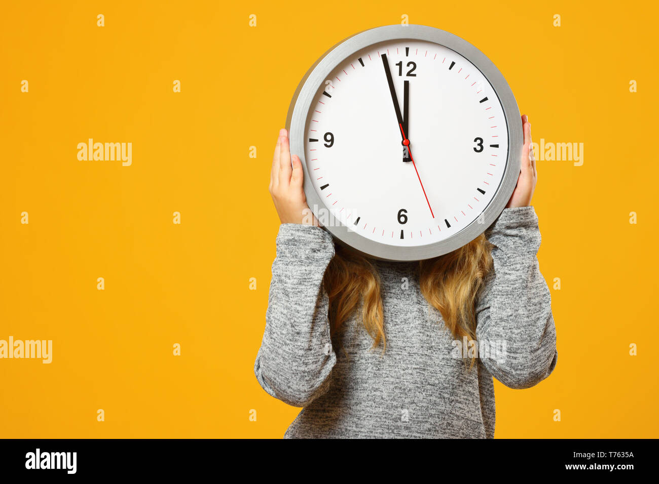 Little child girl holding a big clock on a yellow background. The ...