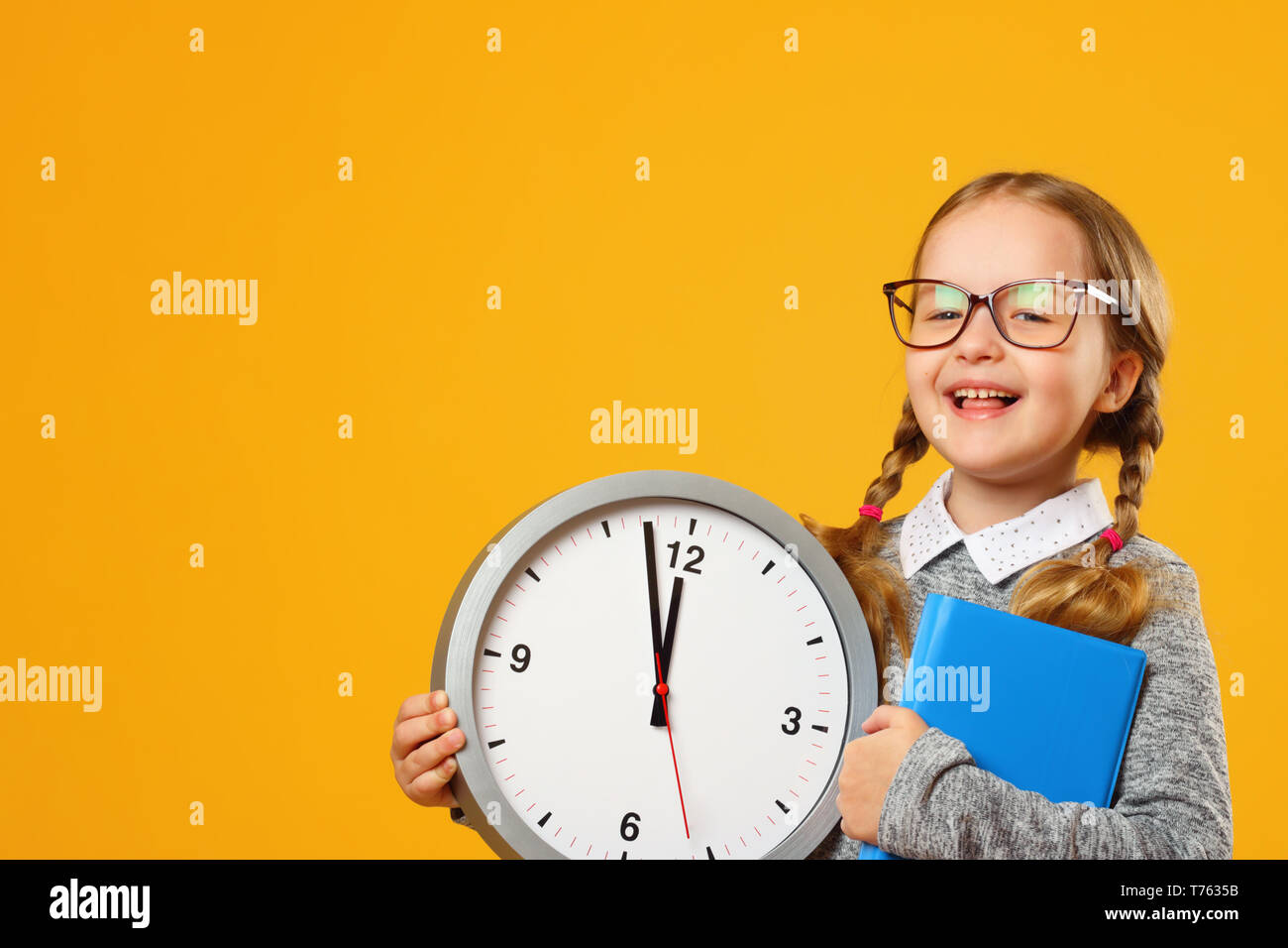 Little girl schoolgirl holds a big clock on a yellow background. The ...