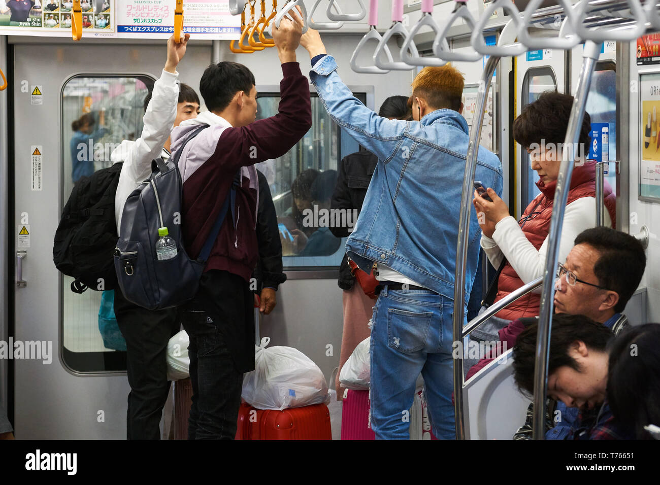 Young men with luggage riding the Tsukuba Express train in Tokyo, Japan ...