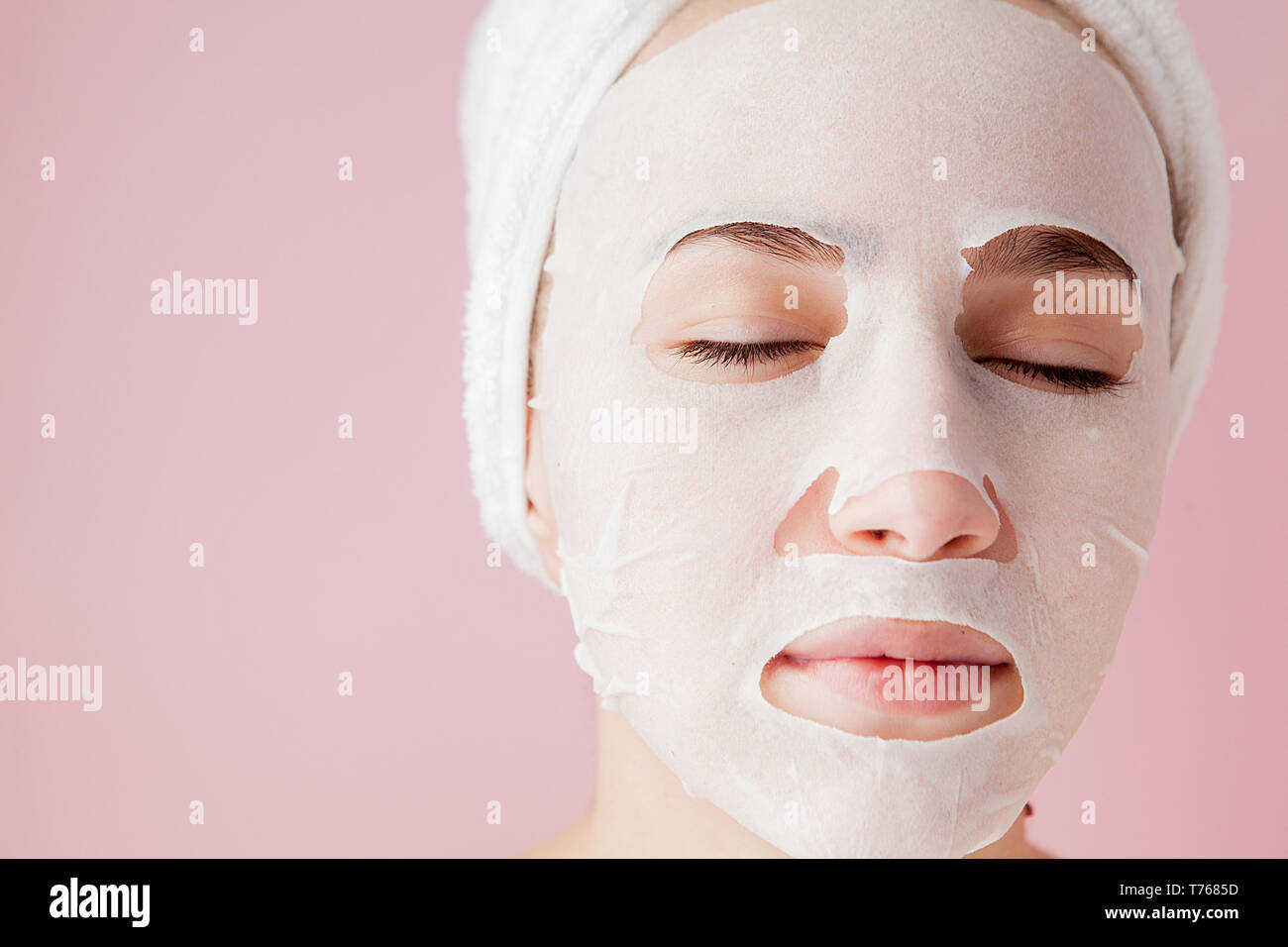Beautiful young woman is applying a cosmetic tissue mask on a face on a ...
