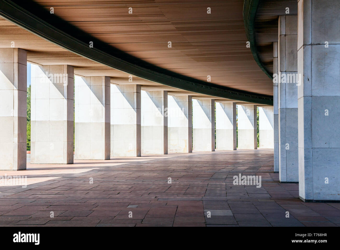 Bent columnade with white columns in sunshine, a wooden ceiling and ...
