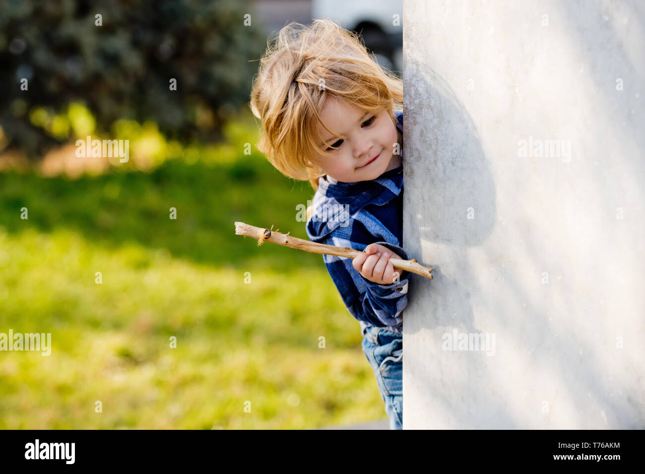 Boy with blond hair with stick smile at wall corner Stock Photo - Alamy